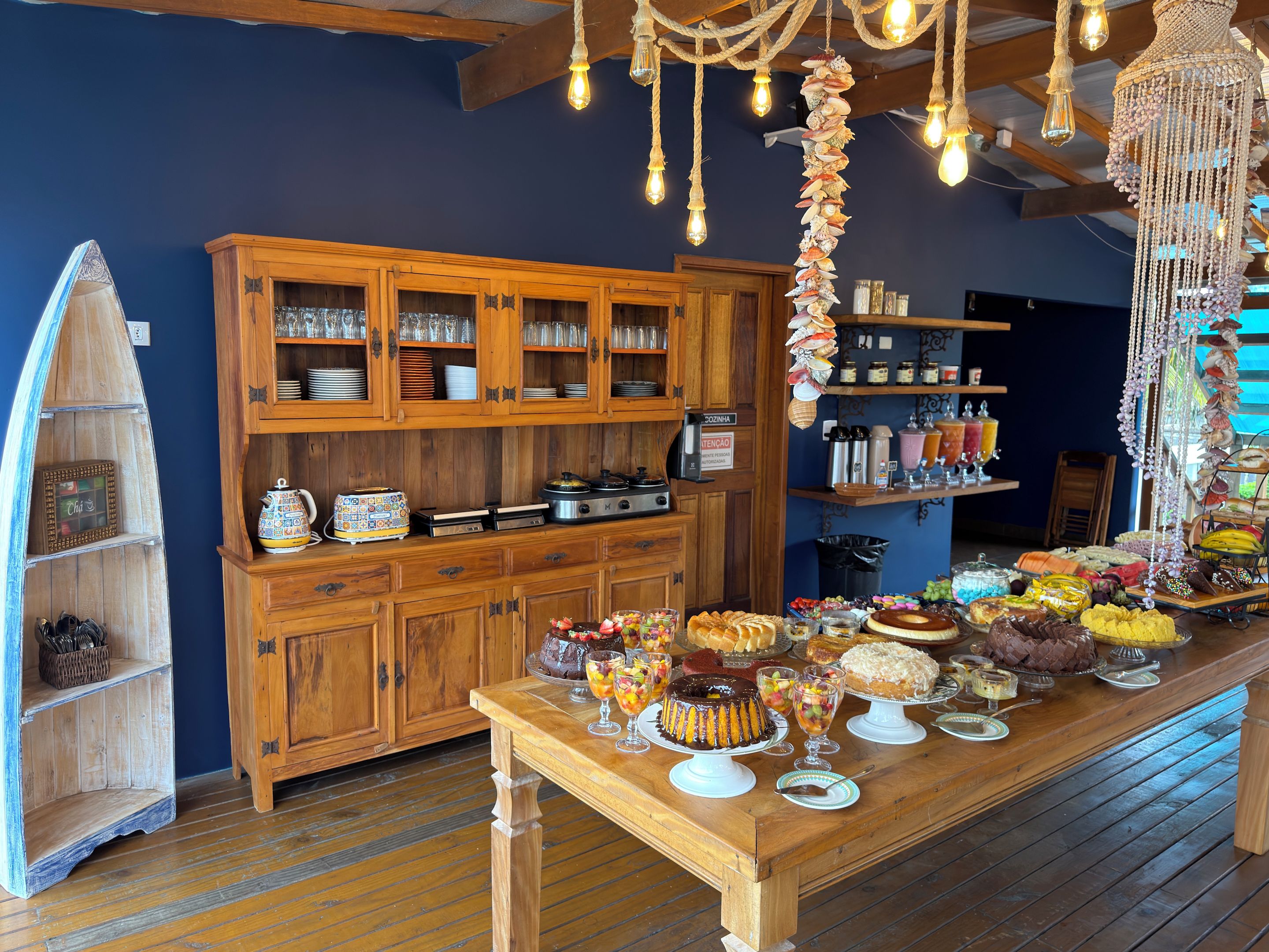 Buffet de madeira com diversos doces e aparador de madeira com copos.