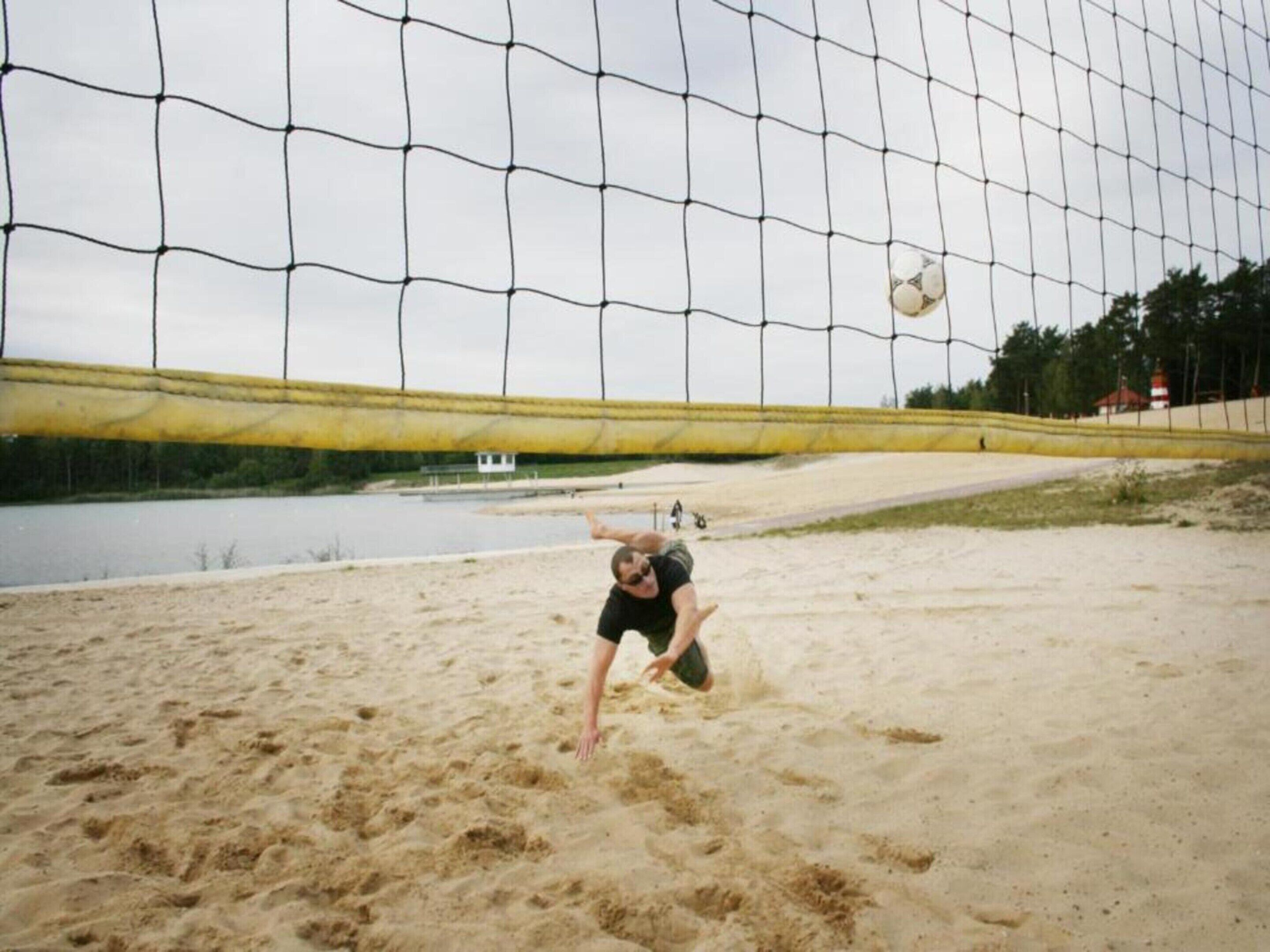 Uma rede de voleibol com quadra de areia e um corpo d'água ao fundo.