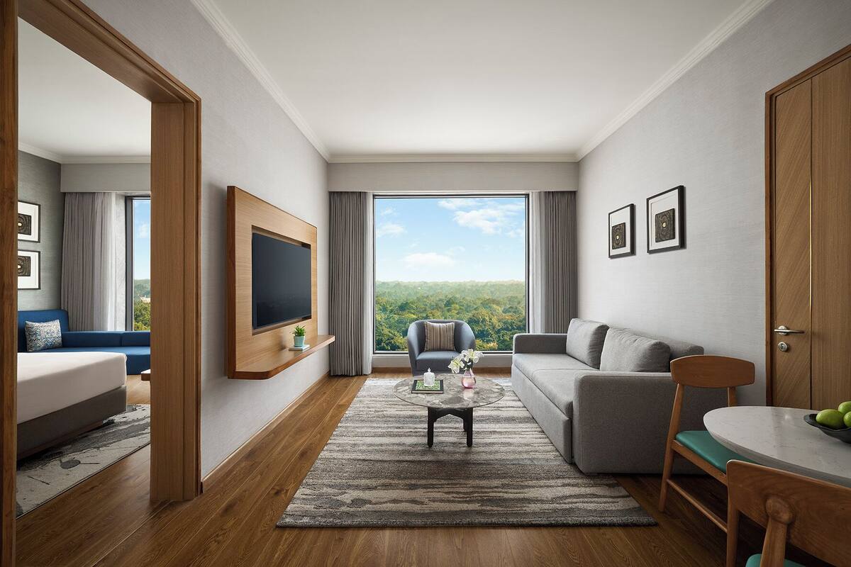 Uma sala de estar moderna com uma televisão grande, um sofá, uma mesa de centro e vista para o exterior.