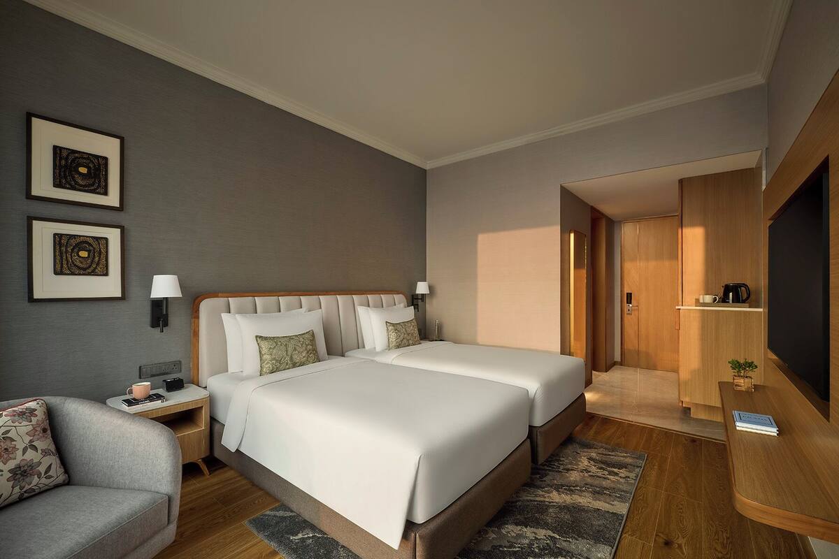 Quarto de hotel com duas camas, um sofá, uma TV e obras de arte na parede.