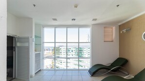 Quarto com uma janela grande, um radiador e duas cadeiras verdes.