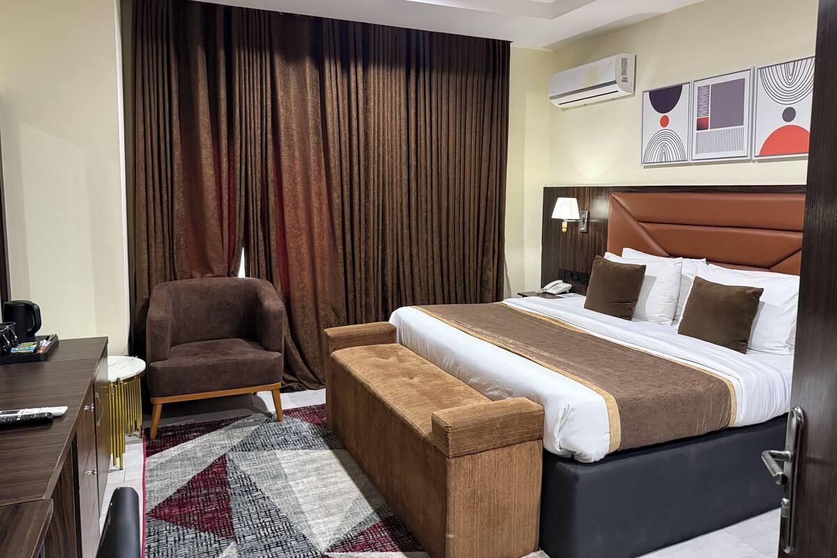 Quarto de hotel com cama, cadeira, escrivaninha e ar condicionado.