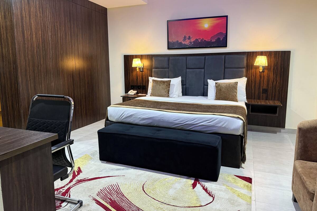 Quarto de hotel com uma cama grande, duas luminárias de cabeceira, uma mesa e uma cadeira.