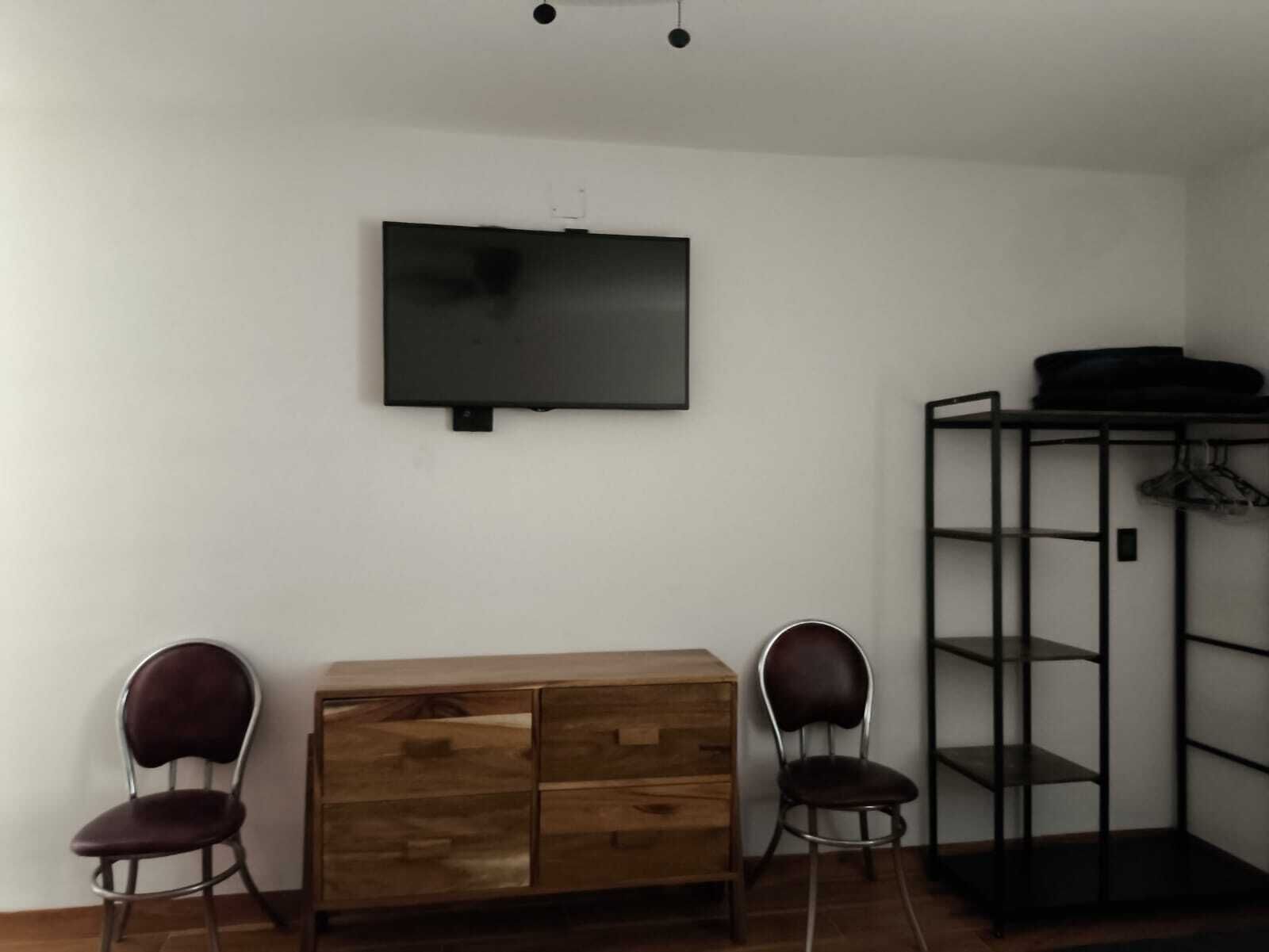 A room with a wooden dresser, two chairs, a TV, and a metal shelving unit.