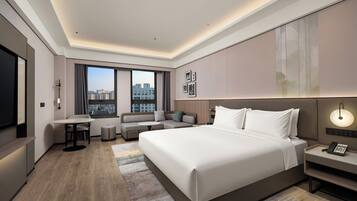 Quarto de hotel moderno com uma cama grande, área de estar, escrivaninha e vista para a cidade.