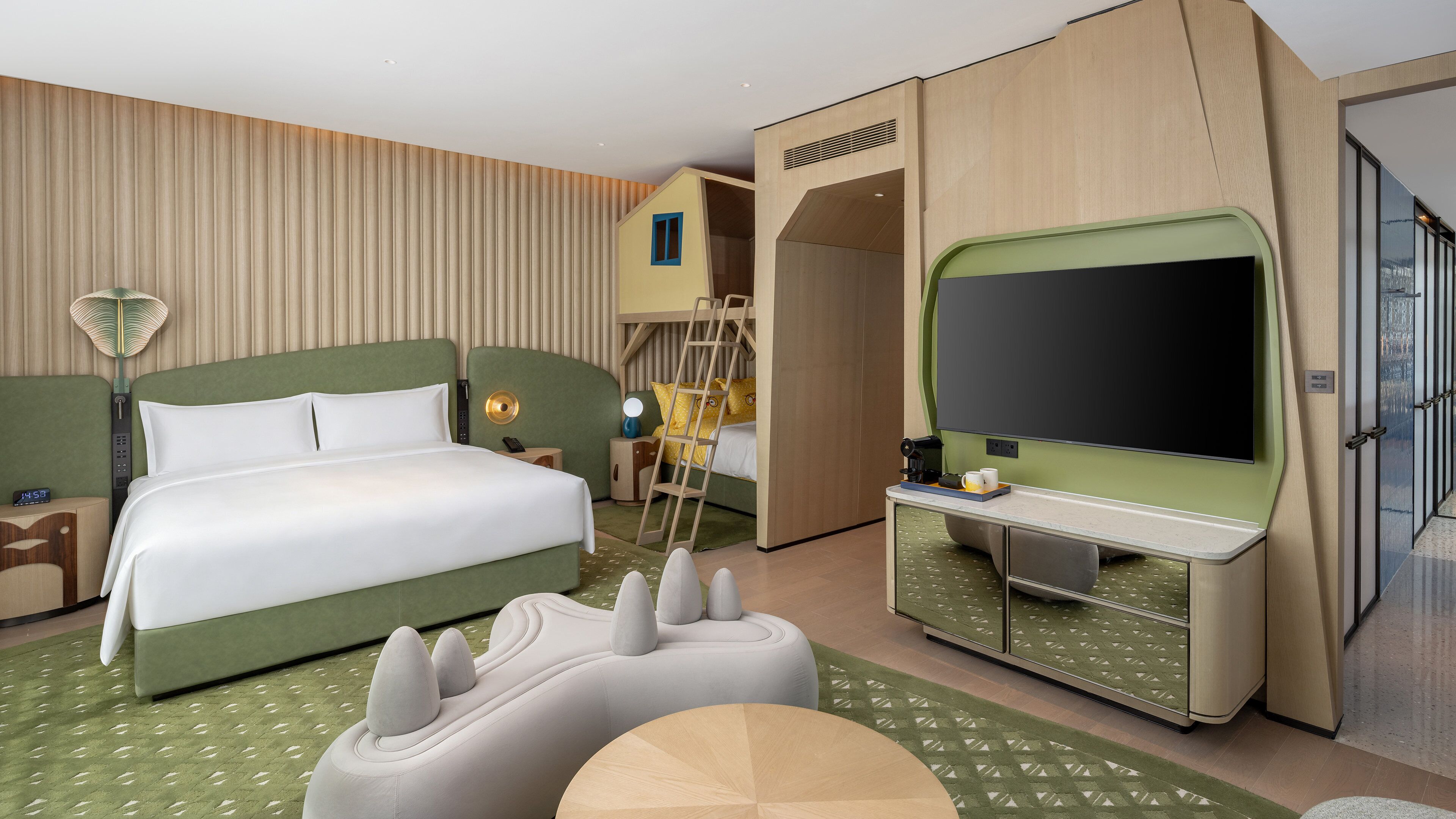 Quarto de hotel com uma cama, uma escrivaninha com televisão de tela plana, uma escada, um criado-mudo e uma luminária de parede.