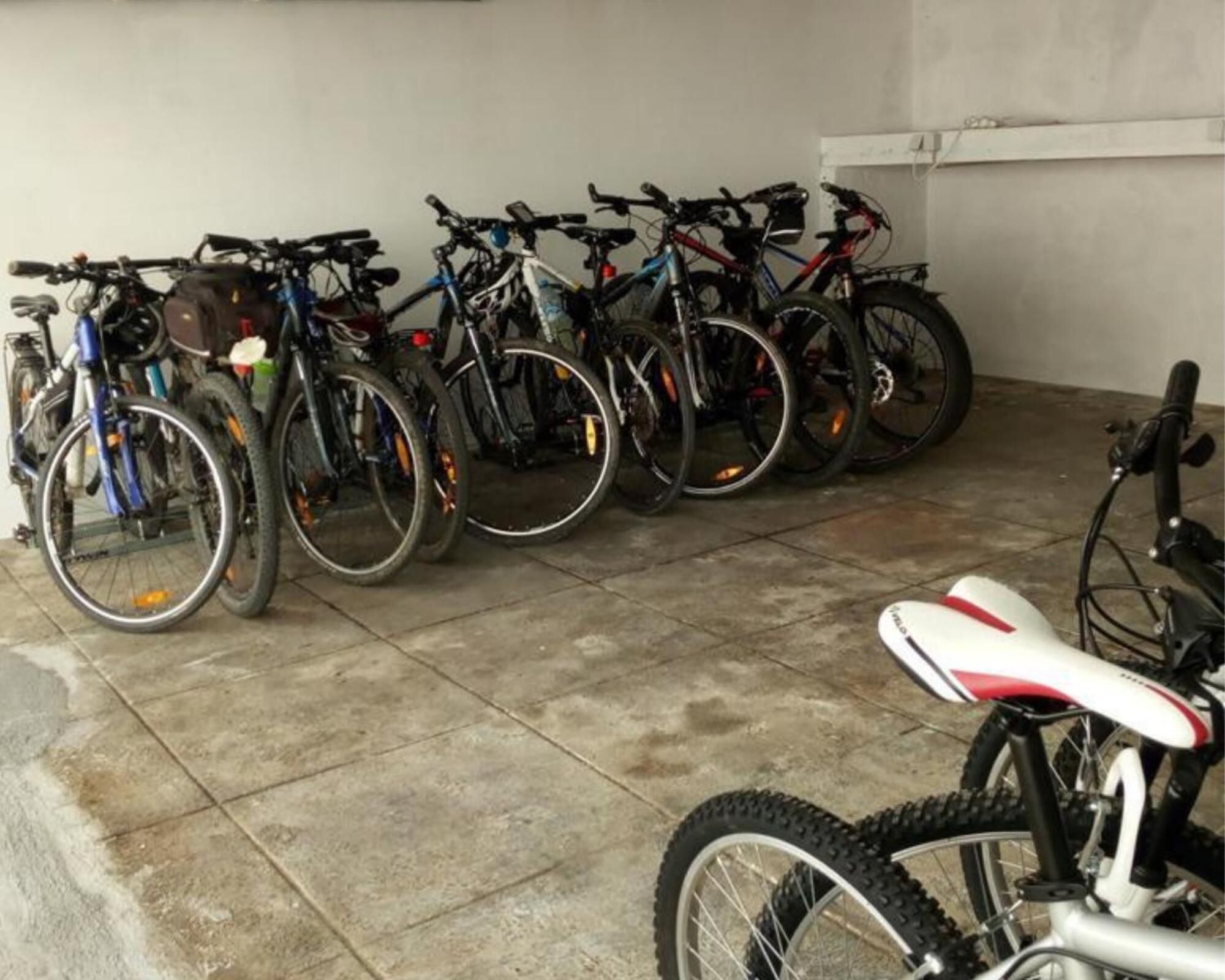 Várias bicicletas estão estacionadas em fila dentro de um espaço com piso de azulejos.
