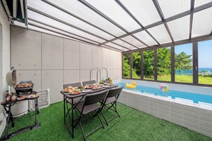 Uma área de refeições ao ar livre com churrasqueira, piscina e vista para o mar.