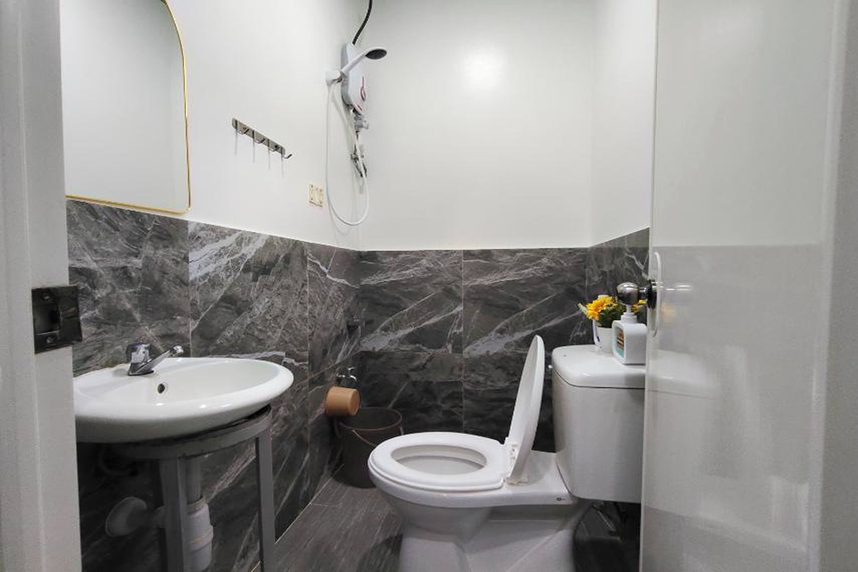 Um banheiro moderno com parede de mármore, pia branca, vaso sanitário e chuveiro.