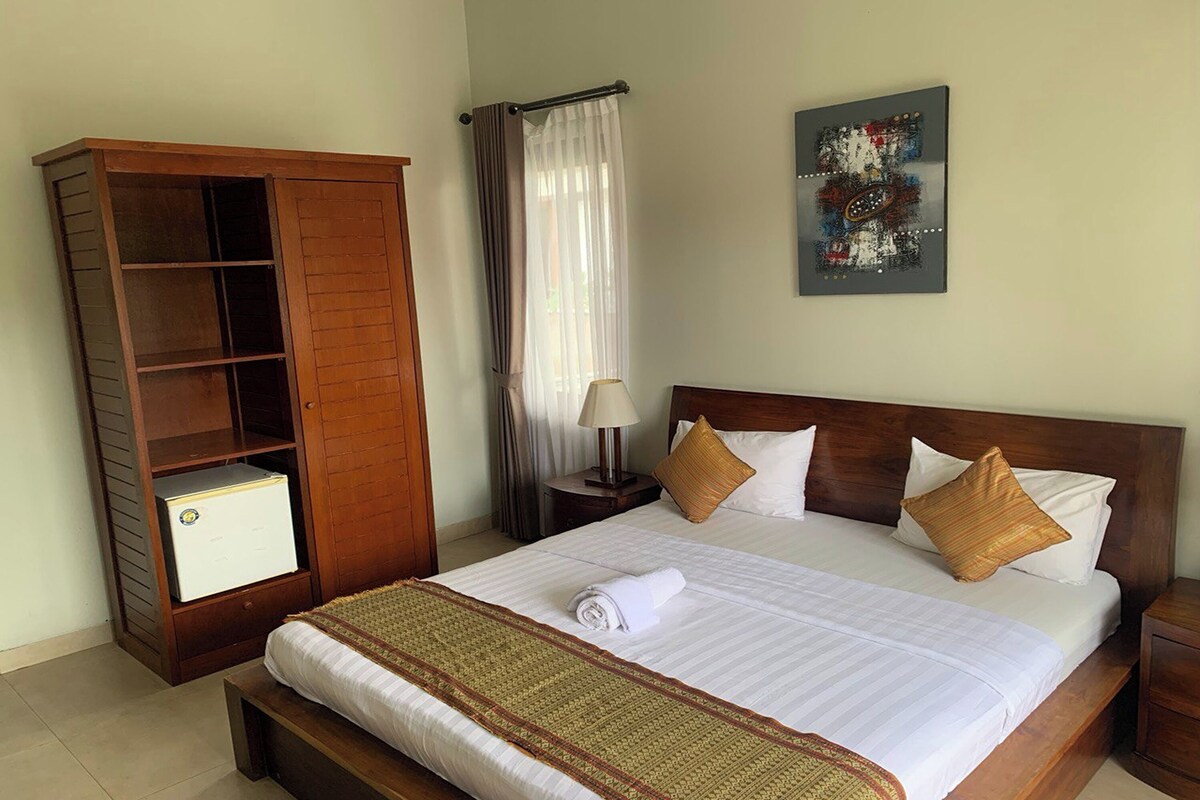 Quarto de hotel com cama, guarda-roupa, mesa de cabeceira, luminária e uma obra de arte na parede.
