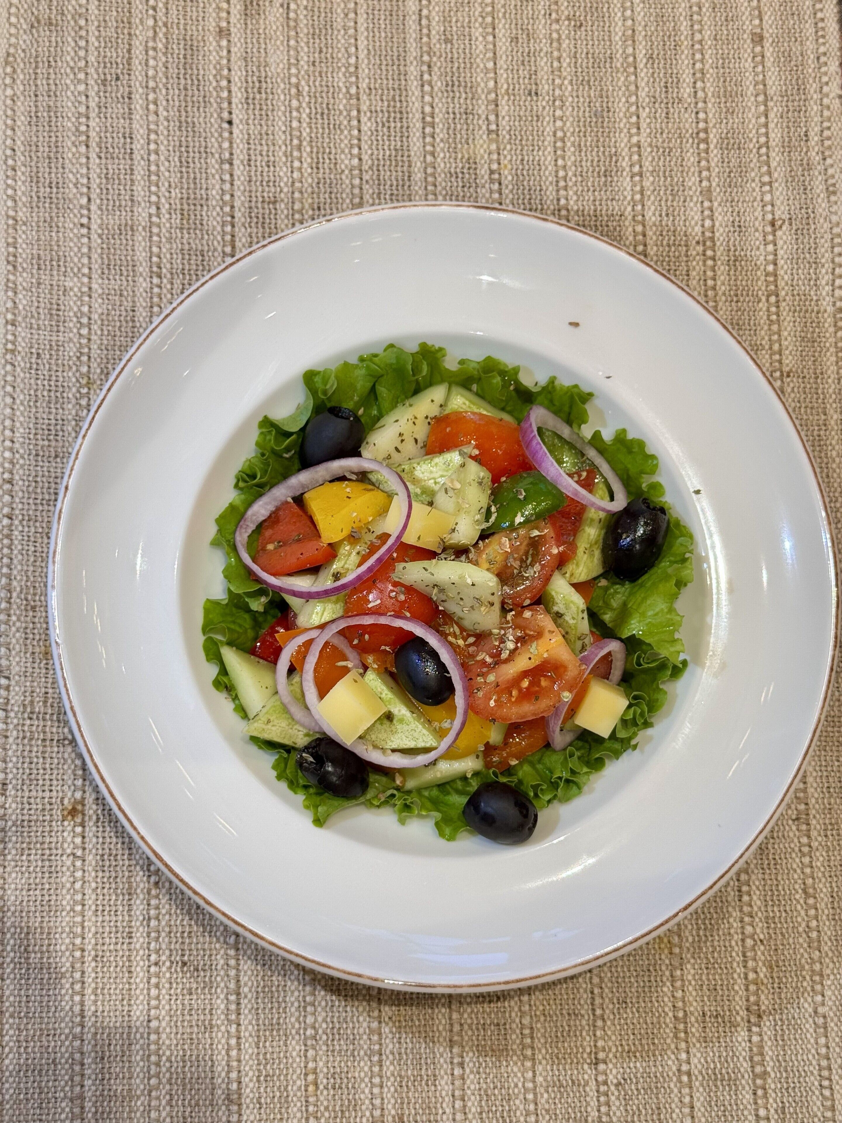 Prato branco com salada sobre fundo de tecido texturizado.