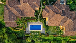Vista aérea de um bairro residencial com várias casas, uma piscina central e jardins bem cuidados.