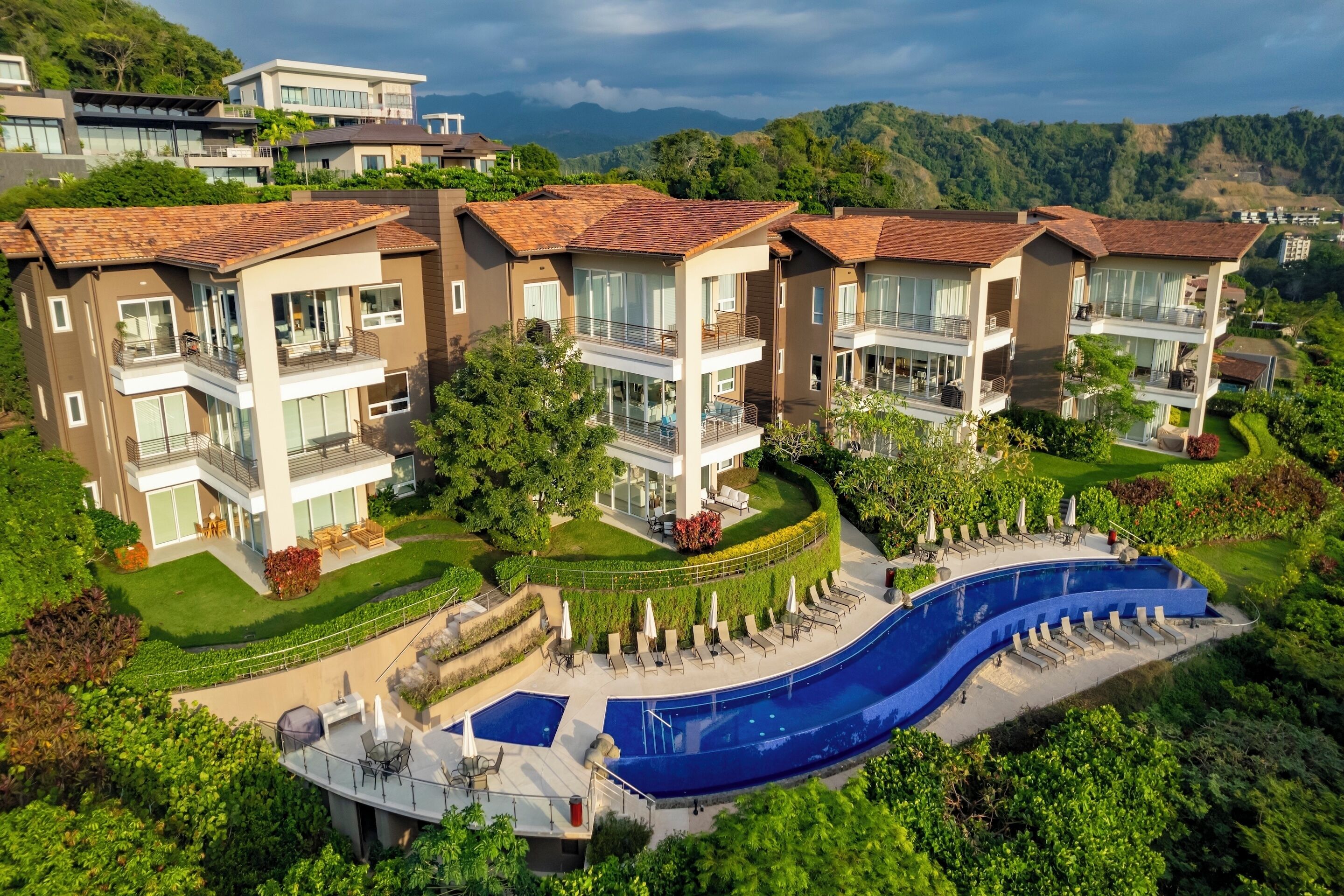 Um complexo residencial moderno com vários edifícios de dois andares, piscina central e jardins bem cuidados.