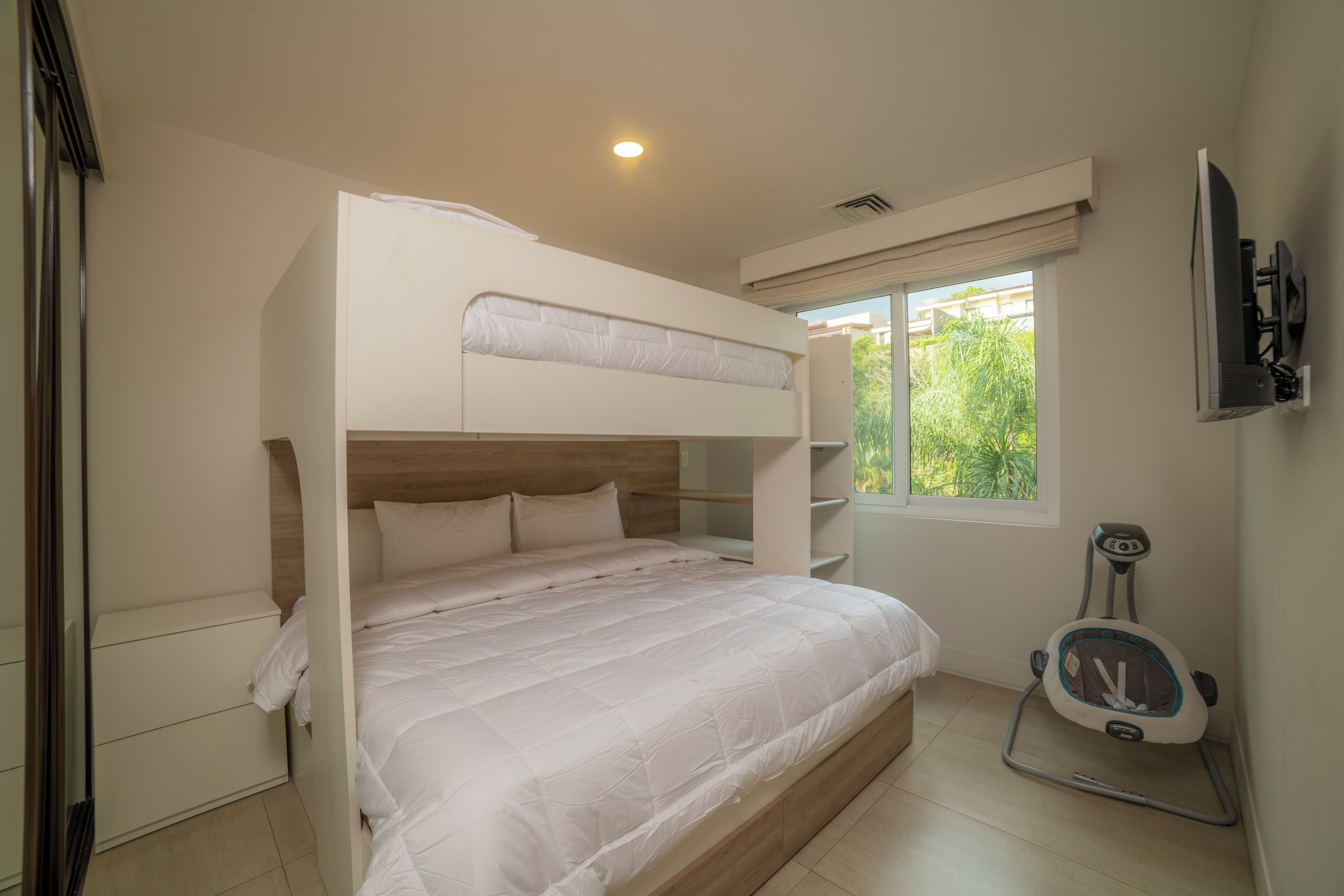 Quarto com beliche, TV fixada na parede, janela com persianas e esteira.