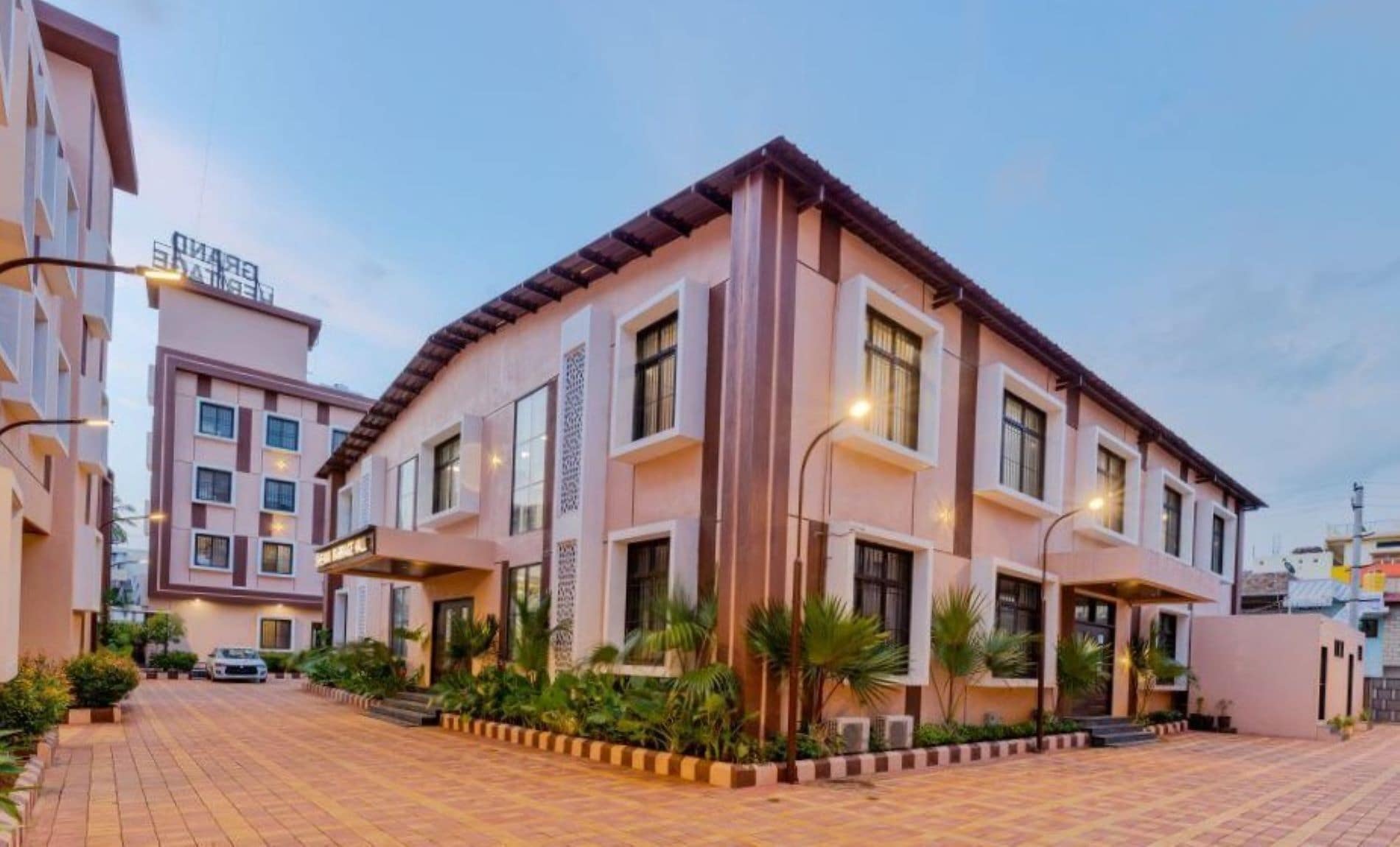 Um hotel de vários andares com design moderno, apresentando um pátio central com palmeiras e um caminho pavimentado.
