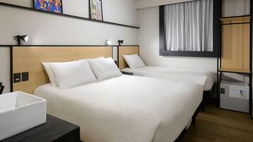 Quarto de hotel com duas camas, uma escrivaninha, um armário pequeno e uma janela com cortinas.
