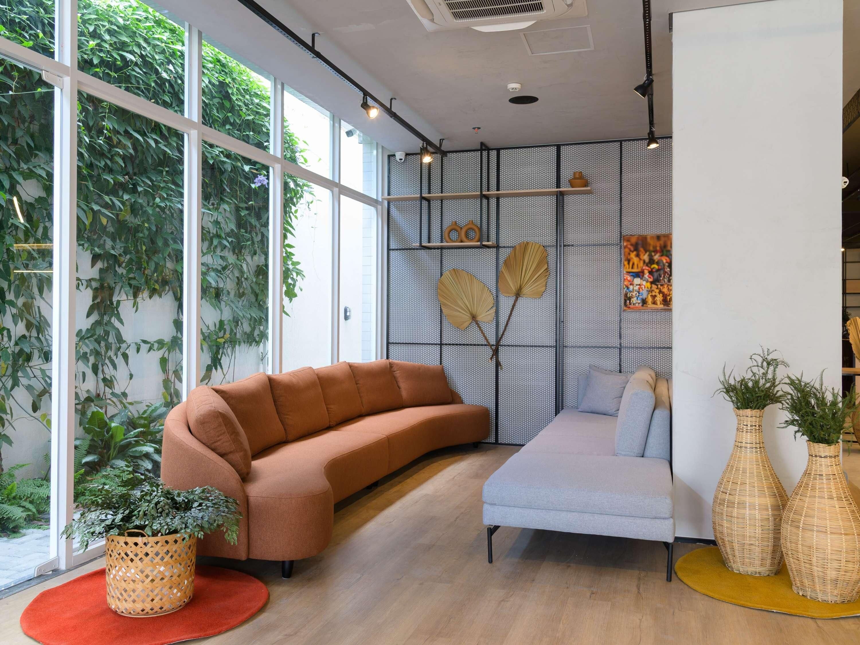 Uma sala de estar moderna com um sofá, uma poltrona e uma grande janela com vegetação lá fora.