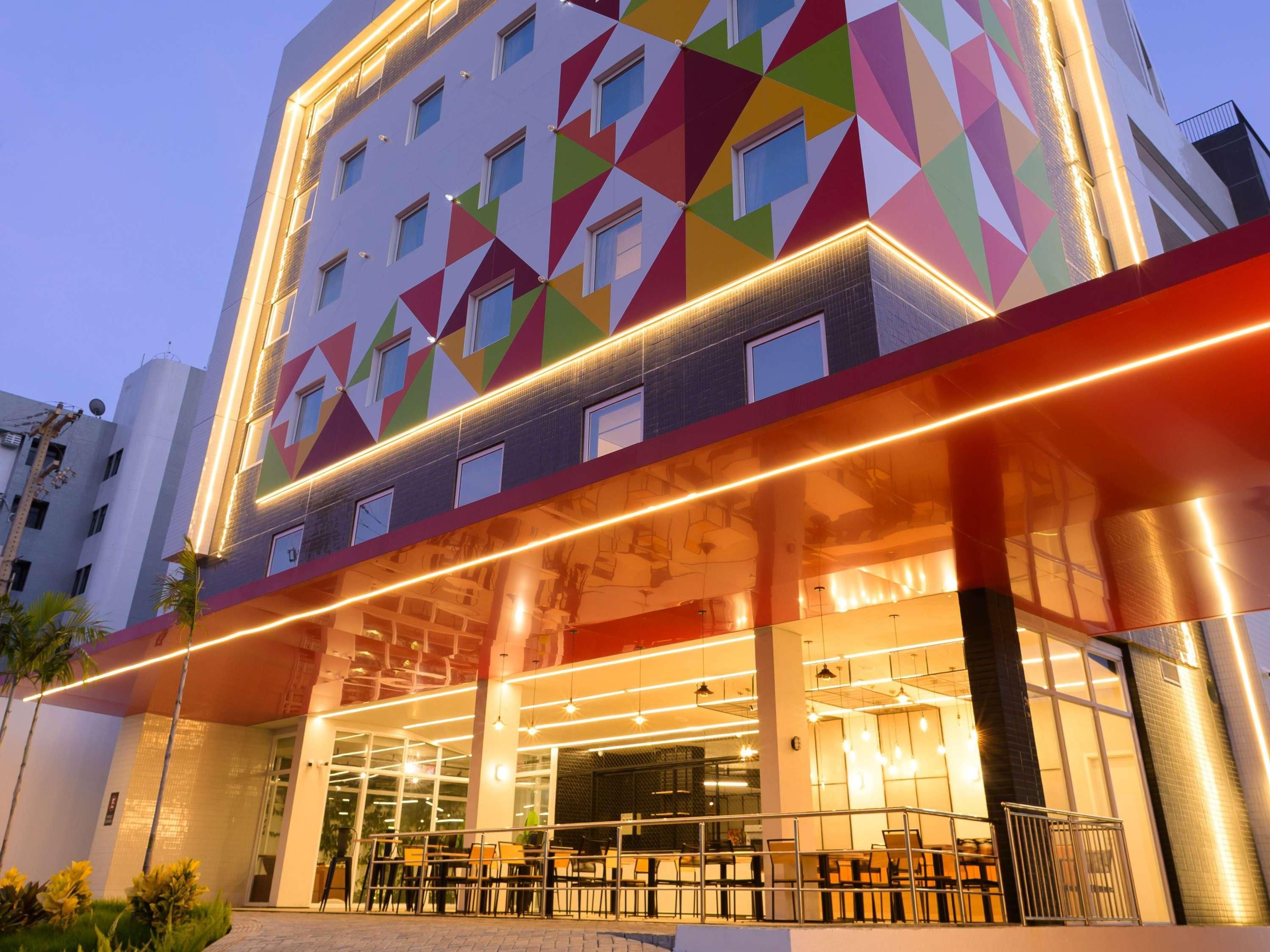Um hotel com vários andares, fachada geométrica colorida, grandes janelas e área de estar externa coberta.