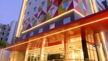 Um hotel com vários andares, fachada geométrica colorida, grandes janelas e área de estar externa coberta.