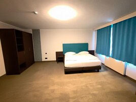 Quarto de hotel com cama, mesa de cabeceira, guarda-roupa e uma grande janela com cortinas.
