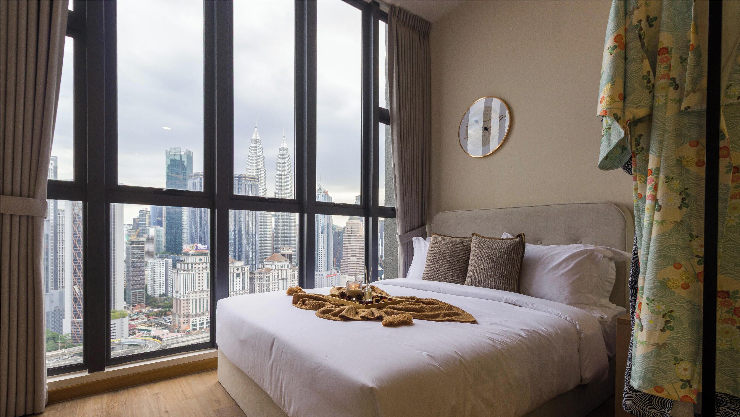 Quarto com uma janela ampla que oferece vista para a cidade, cama com roupa de cama branca e espelho decorativo na parede.