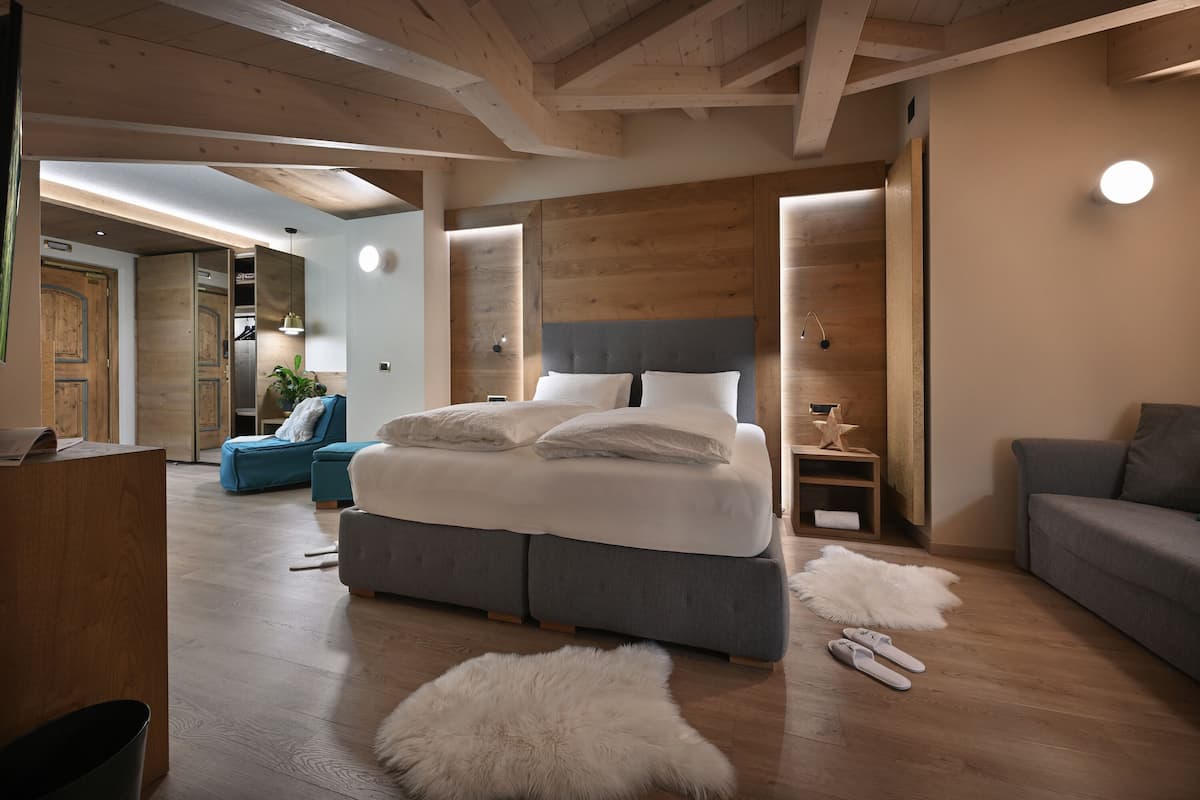 Quarto moderno com uma cama grande, um sofá cinzento e teto de madeira.