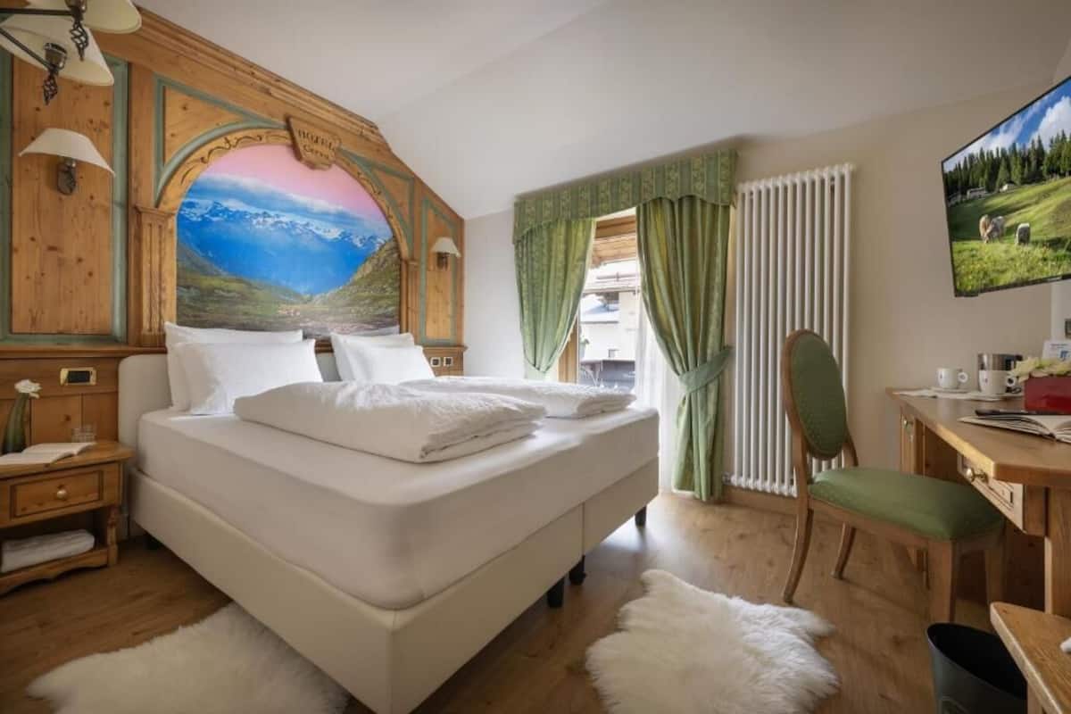 Quarto com cama, escrivaninha, cadeira, quadro e televisão.