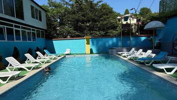 Piscina com espreguiçadeiras, um edifício com amplas janelas e um céu azul límpido.