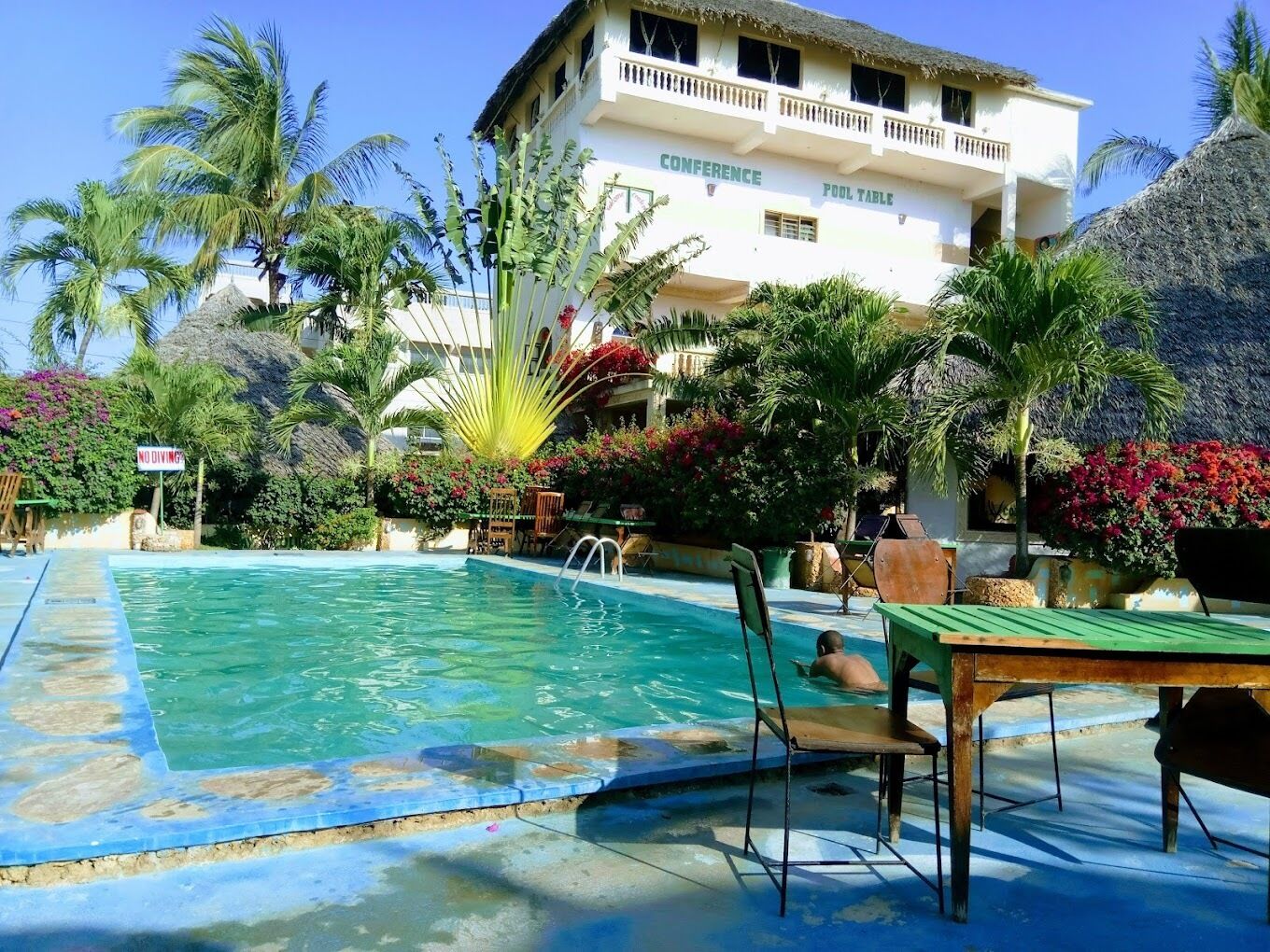 Uma área de piscina com aviso de proibição de mergulho, rodeada por vegetação exuberante e um edifício com a inscrição 'Conference Pool Table'.