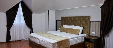 Quarto com piso de madeira, uma cama com cabeceira, mesa de cabeceira e janela com cortinas.