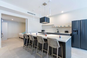 Cozinha moderna com ilha central, banquetas, coifa preta e geladeira de aço inoxidável.
