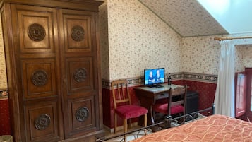 Quarto com guarda-roupa de madeira, uma escrivaninha com computador, uma cama e um claraboia.