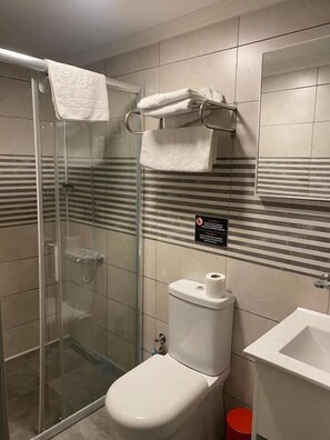 Casa de banho moderna com chuveiro envolto em vidro, sanita e lavatório.