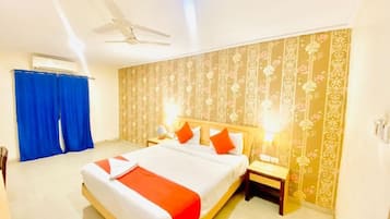 Quarto de hotel com uma cama grande, duas mesas de cabeceira, um ventilador de teto e papel de parede floral.