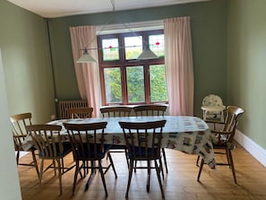 Uma sala de jantar com mesa, cadeiras, uma janela com cortinas e um radiador.