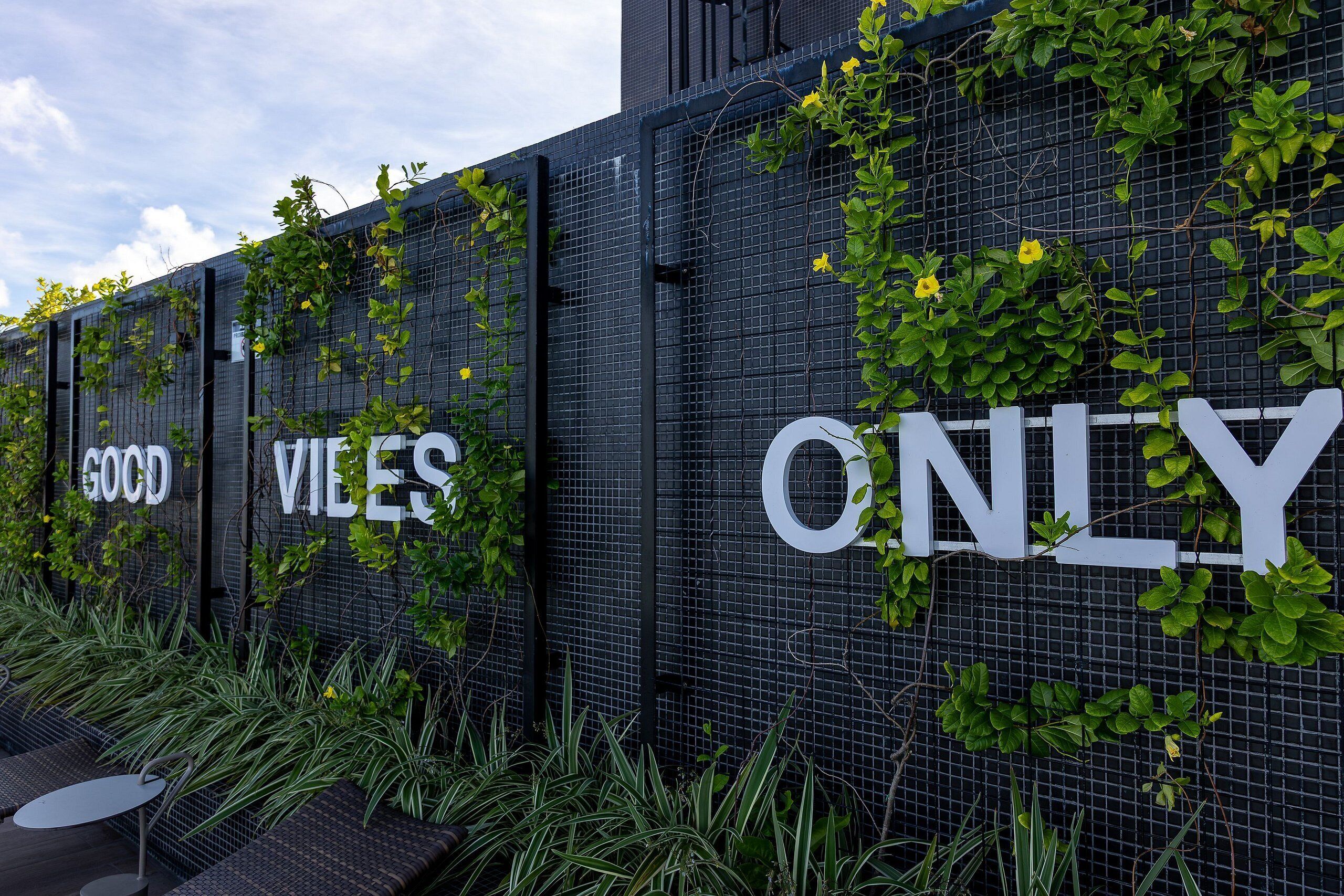 Paredes cobertas por plantas trepadeiras com a frase 'GOOD VIES ONLY' em letras grandes.