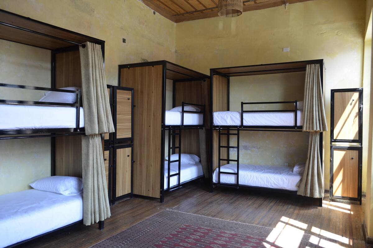 Quarto em dormitório com beliches, piso de madeira e tapete vermelho estampado.