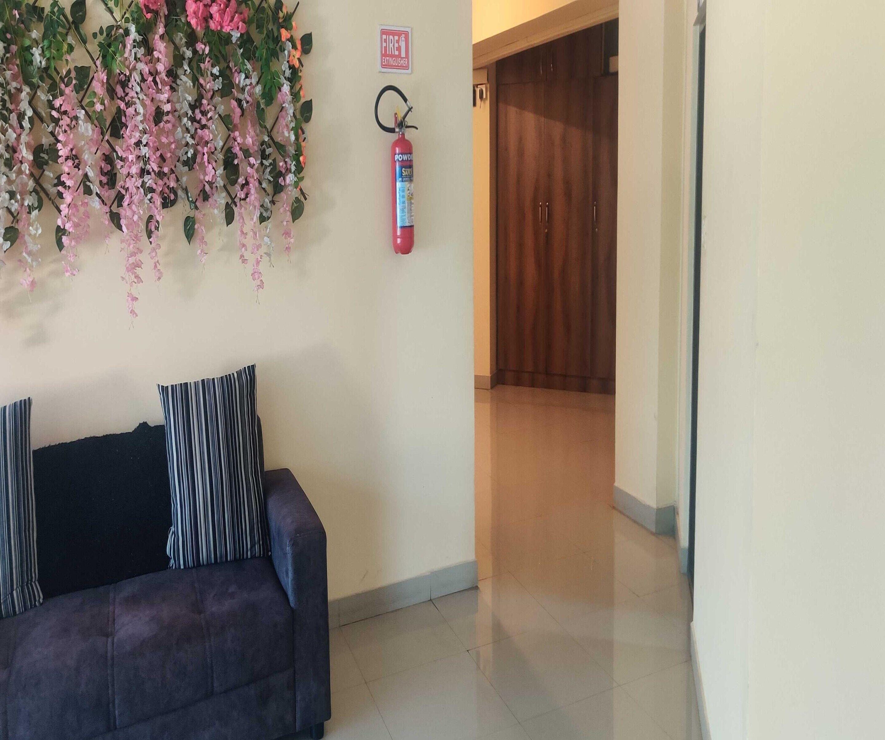 Um corredor com um extintor, um sofá com almofadas listradas e uma porta no final.