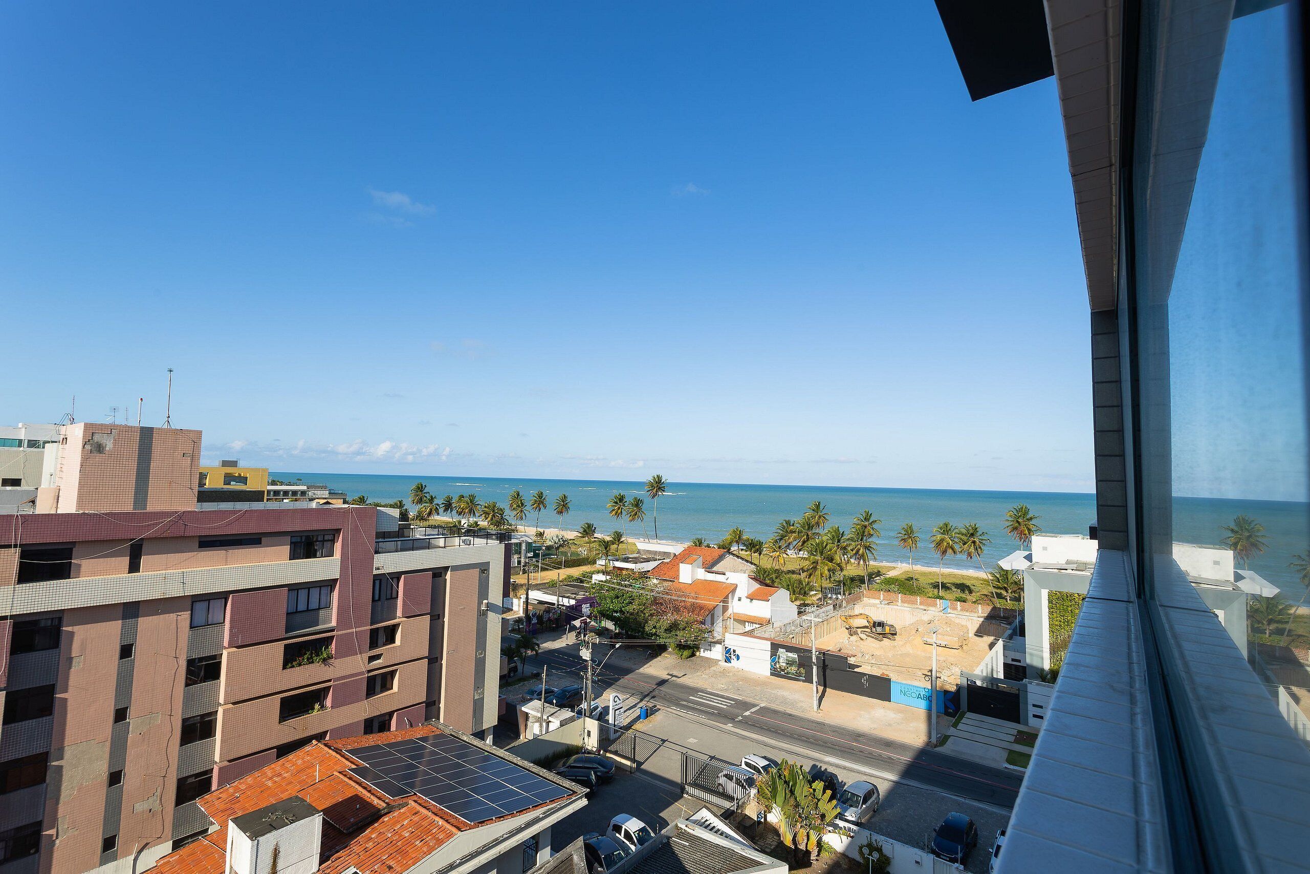 Vista de um edifício alto com vista para uma área costeira, palmeiras, uma praia e o oceano.