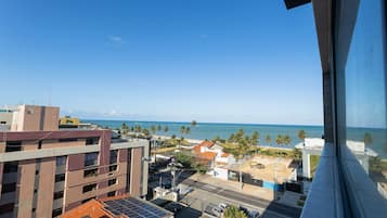 Vista de um edifício alto com vista para uma área costeira, palmeiras, uma praia e o oceano.
