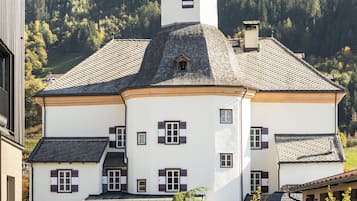Um edifício grande e branco com uma cúpula marcante e várias janelas, rodeado por um jardim bem cuidado e uma paisagem montanhosa.