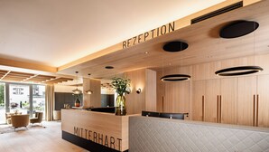 Uma área de recepção com balcão de madeira, uma planta e uma placa com a inscrição 'RECEPTION'.