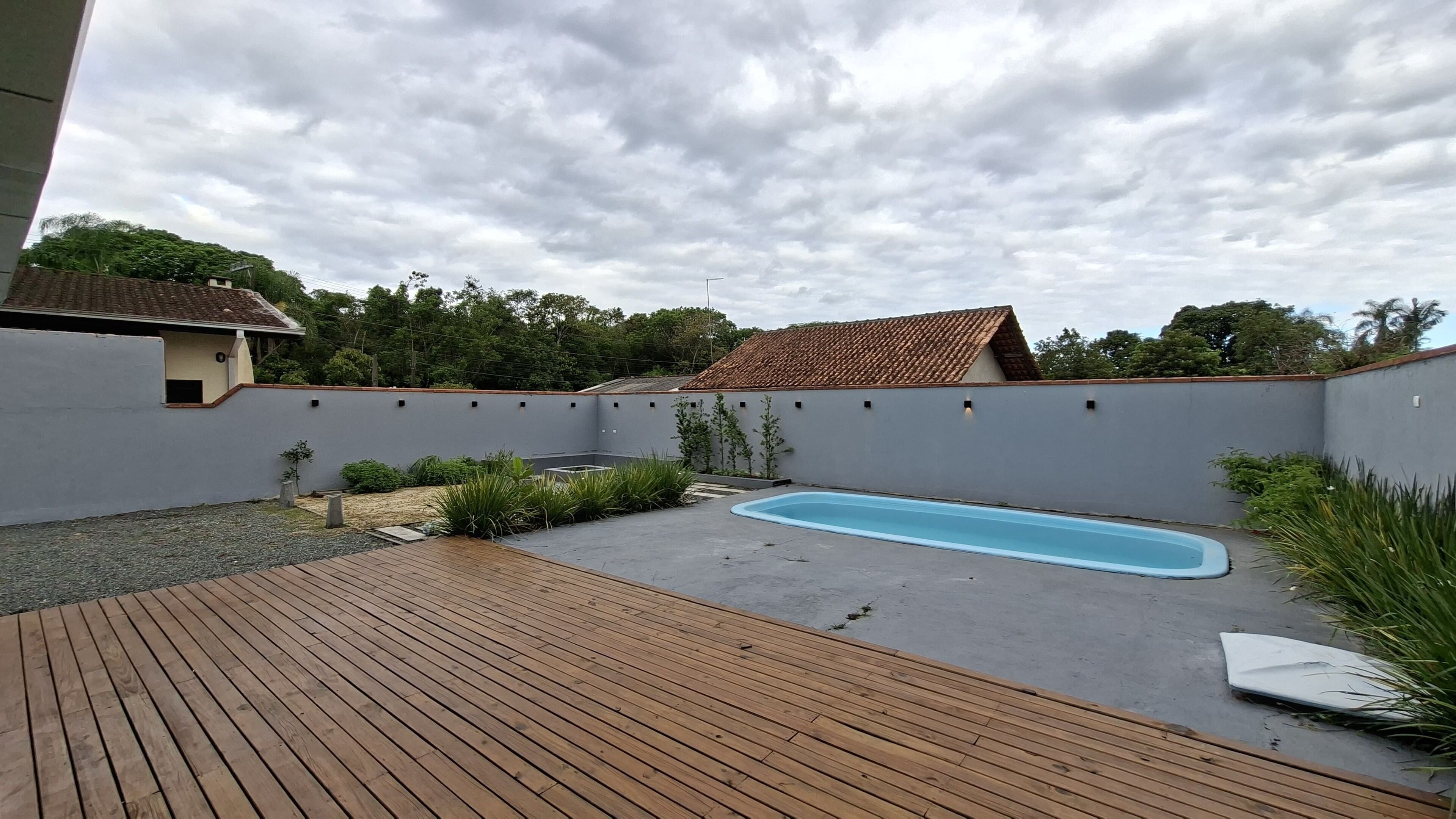 Um quintal com piscina, deck de madeira e uma parede cinza.