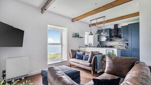 Uma sala de estar moderna com sofá de couro, área de jantar e cozinha ao fundo, e uma grande janela com vista.