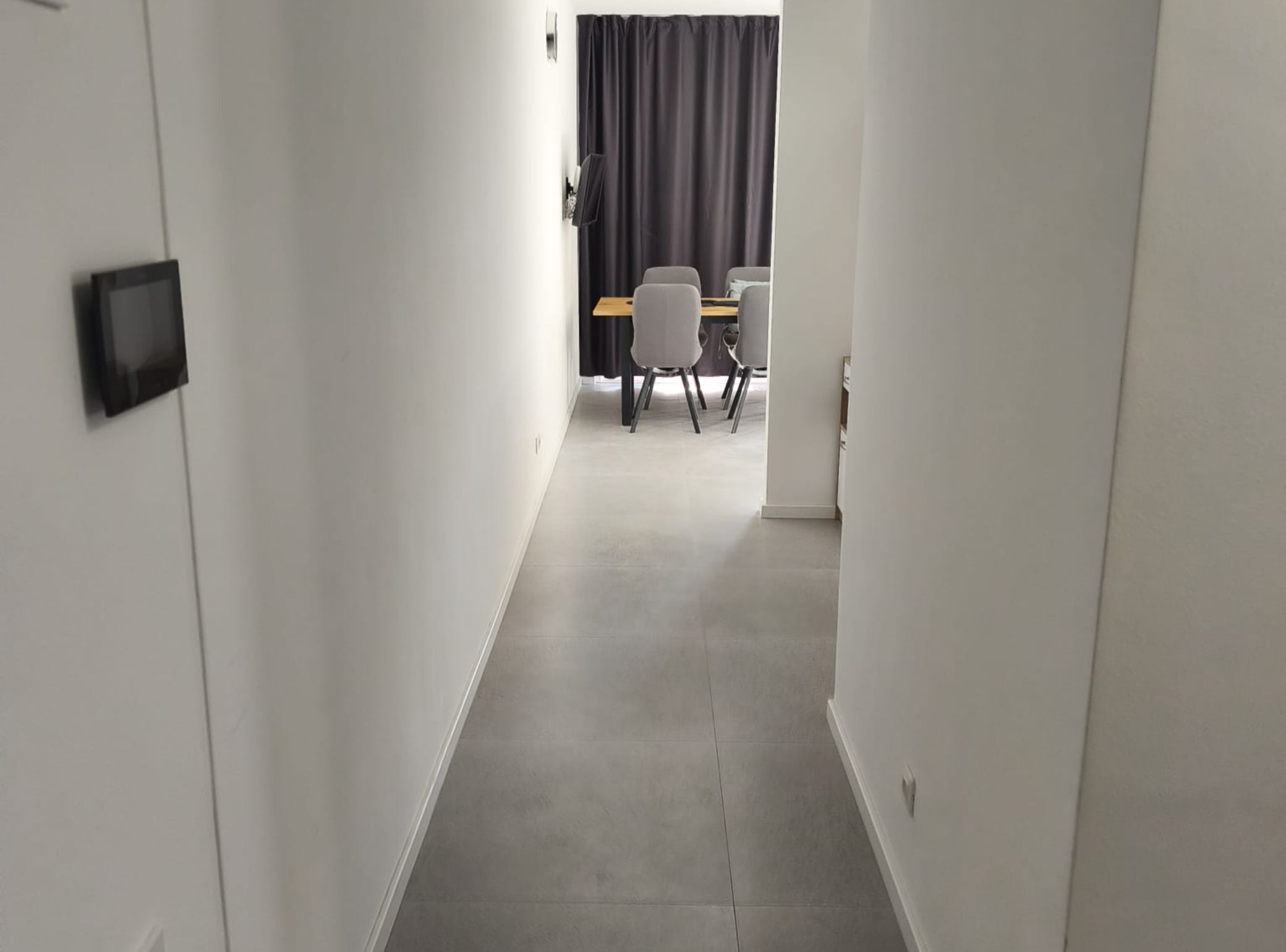 Um corredor estreito com piso nivelado, TV na parede e, ao fundo, um espaço de jantar com cadeiras e mesa.