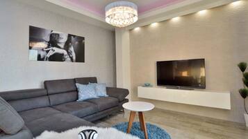 Uma sala de estar moderna com um sofá cinzento, televisão na parede, candelabro e tapete azul.