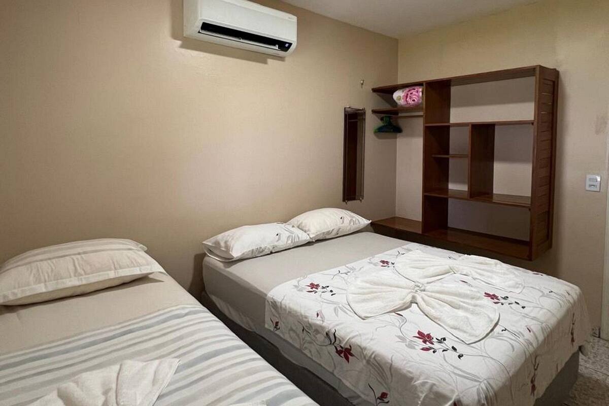 Quarto de hotel com duas camas, um ar condicionado, um espelho e uma prateleira de madeira.