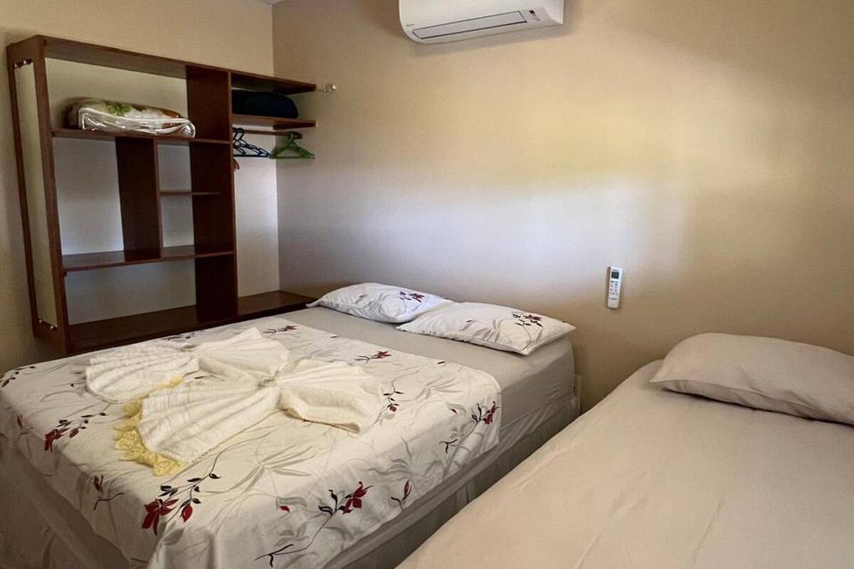 Quarto com duas camas, um guarda-roupa, ar condicionado e telefone ao lado da cama.