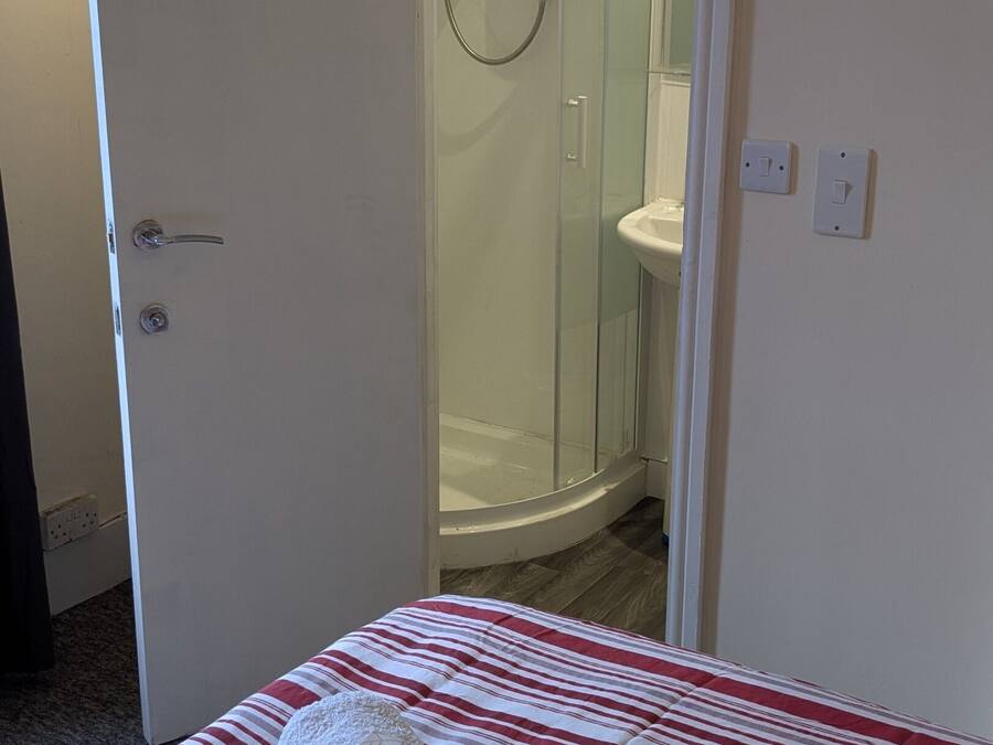 Quarto de hotel com cama, área de chuveiro e uma porta.
