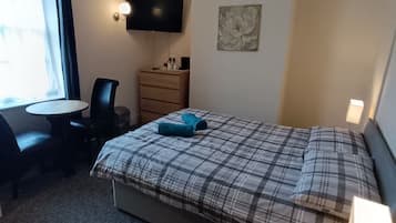 Quarto de hotel com cama, escrivaninha, poltrona, cômoda, televisão e janela.